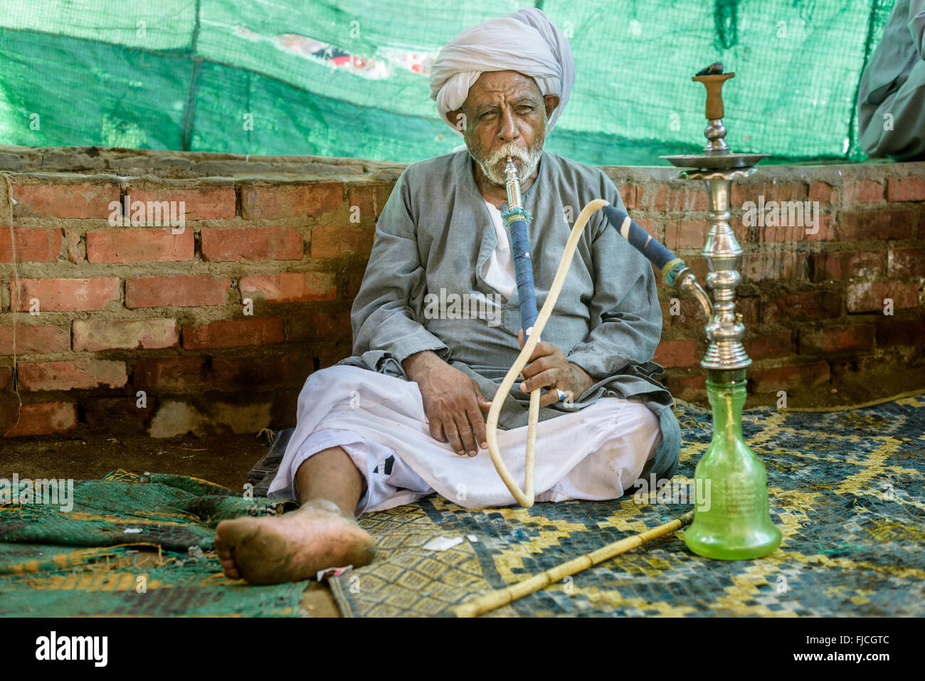 Old muslim man smoking from a water pipe sitting on a rug at Daraw ...