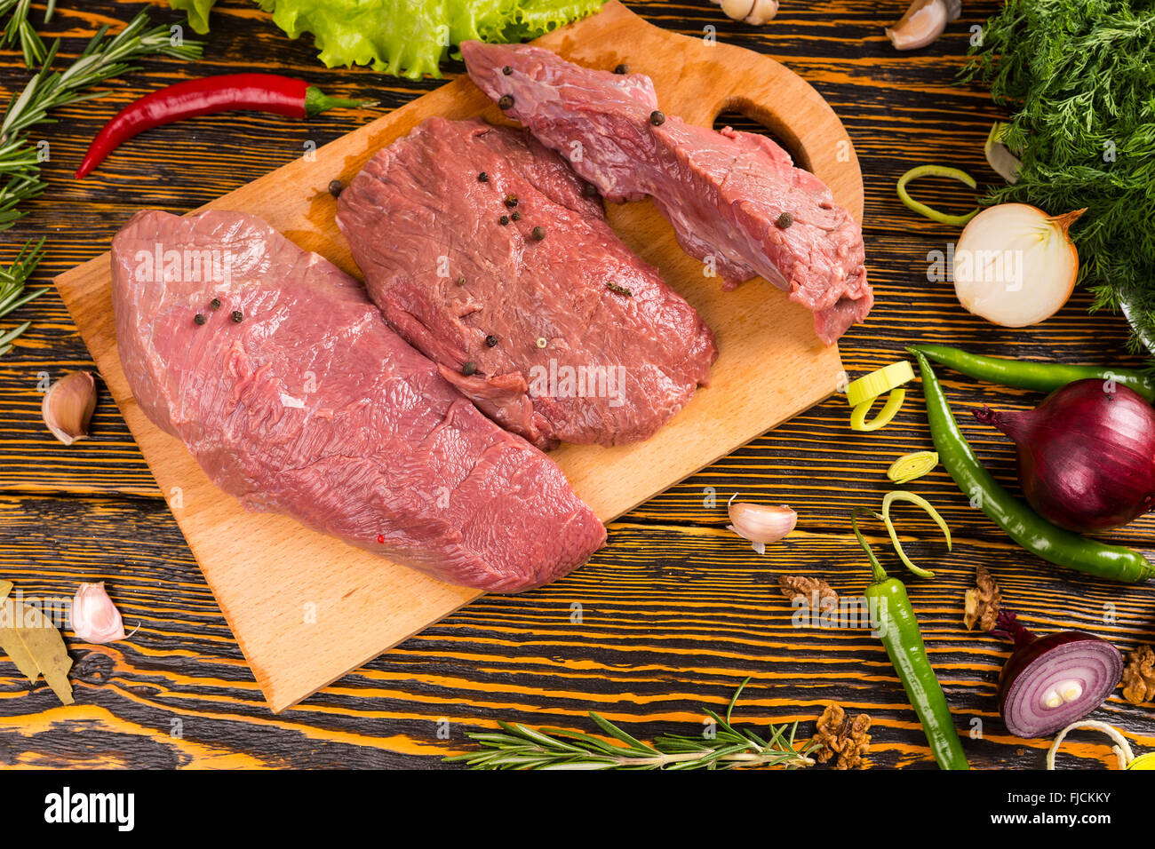 Top down view of raw red meat on cutting board surrounded by peppers ...
