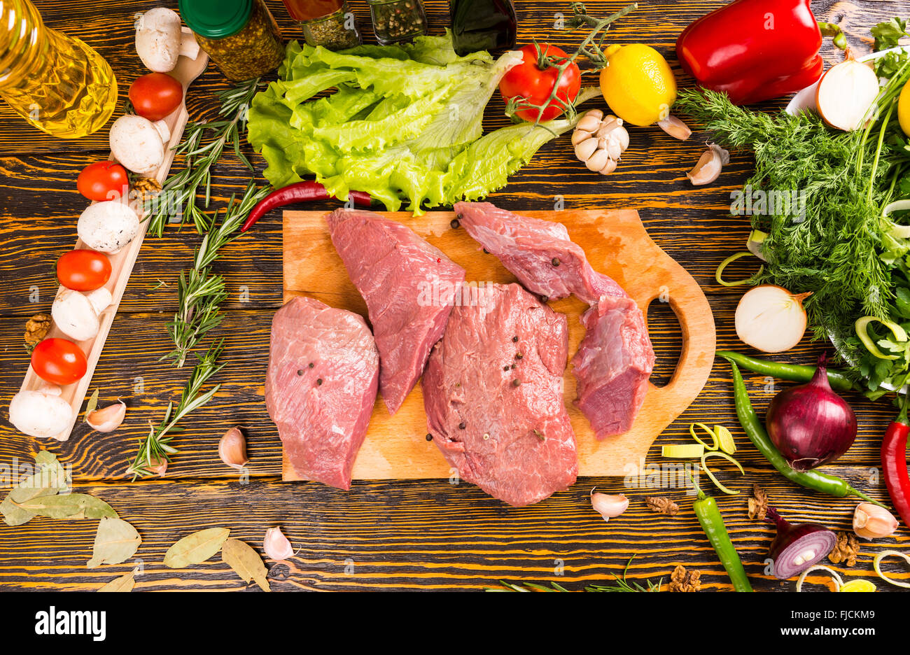 Above view on four cuts of raw red meat over wooden table surrounded by ...