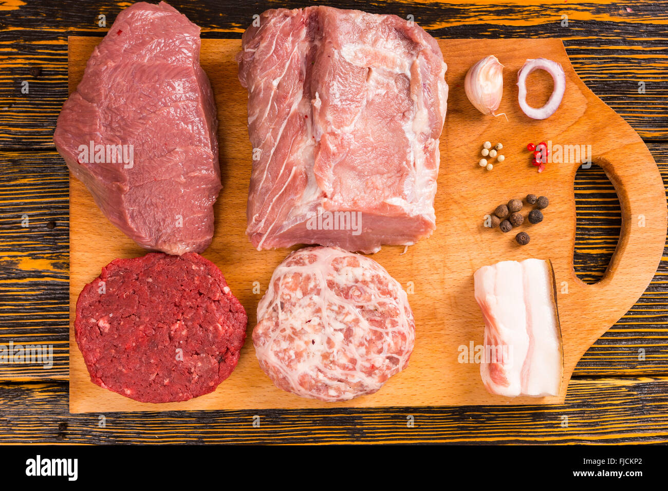 Single wooden cutting board with raw meat pieces and samples of garlic ...