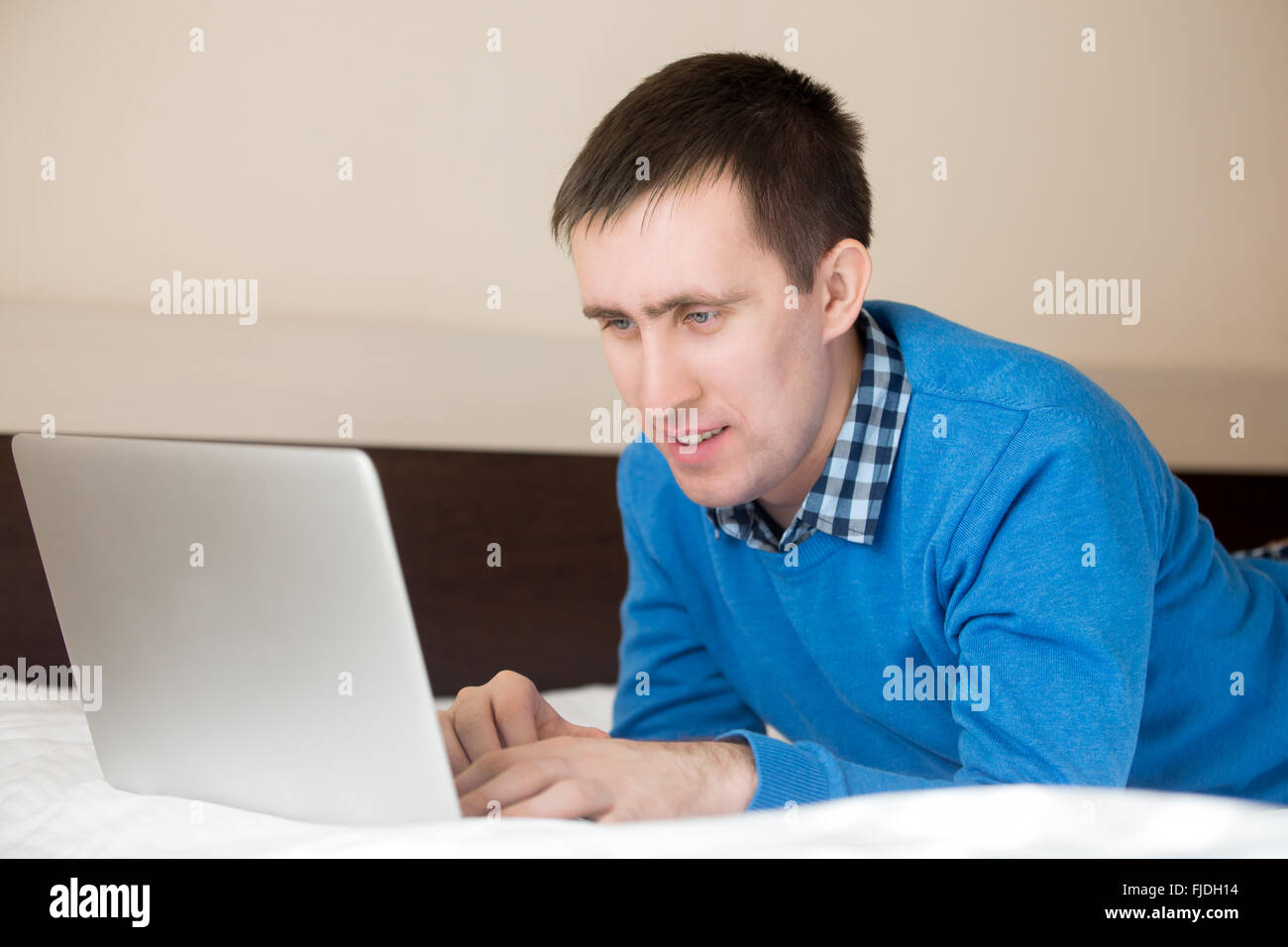 Portrait of smiling casual attractive young man lying on bed using ...