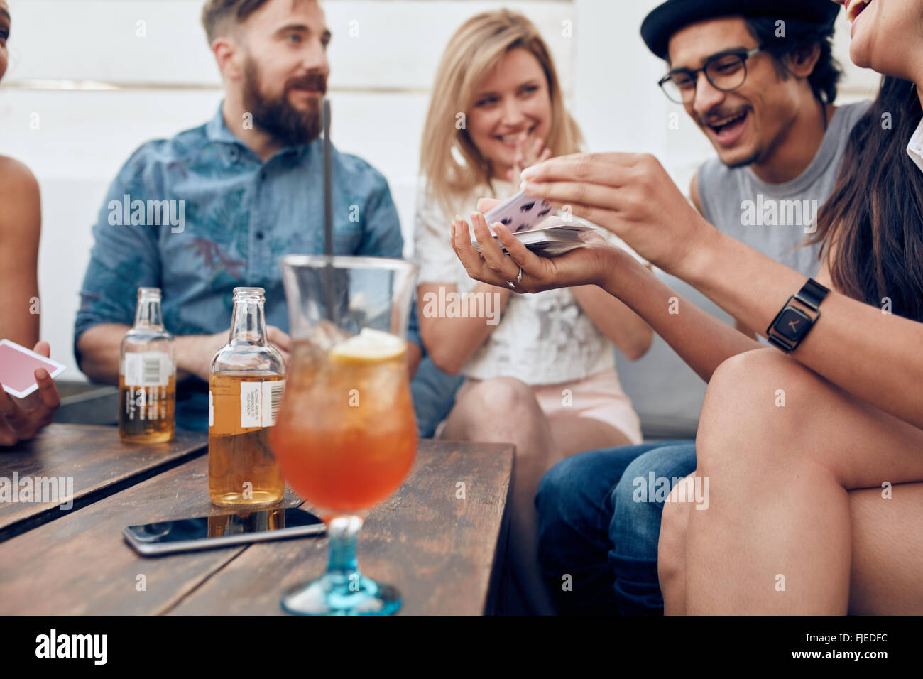 Group of young people sitting at a wooden table and playing cards ...