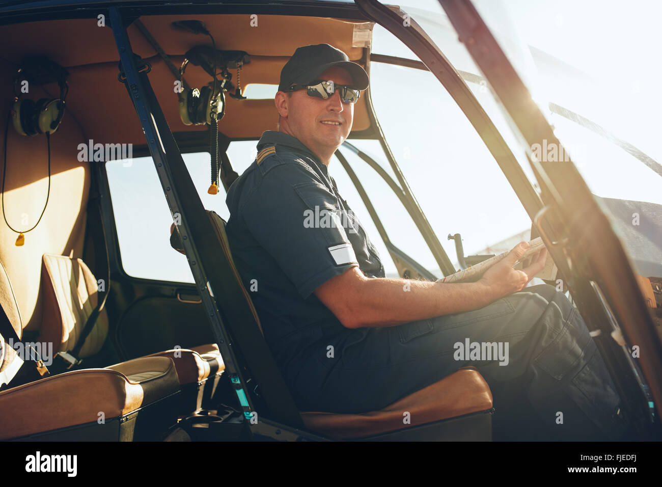 Portrait of happy male pilot sitting in the cockpit of a helicopter ...