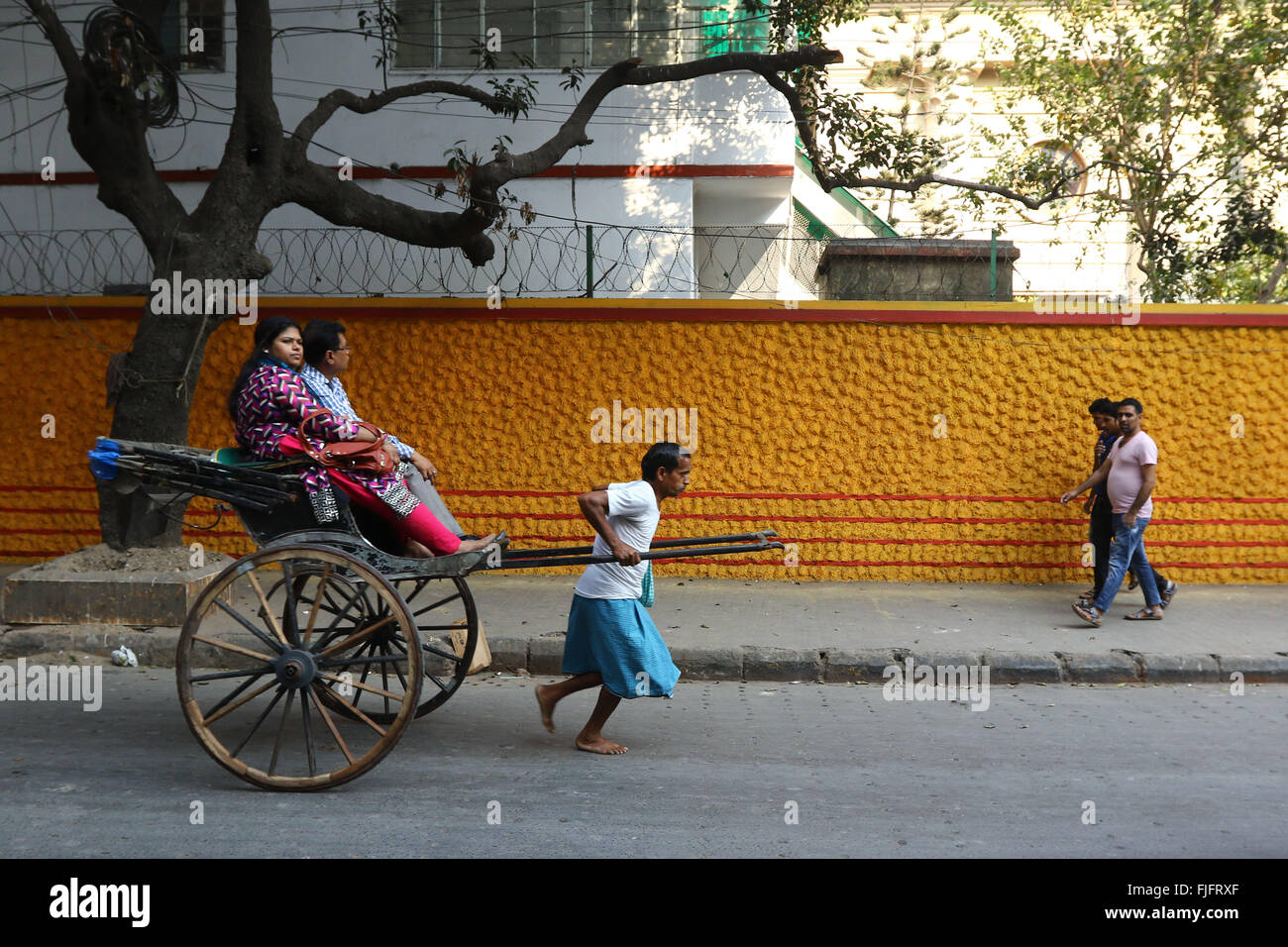 Hand pulling rickshaw puller pulling with passenger walks past a ...