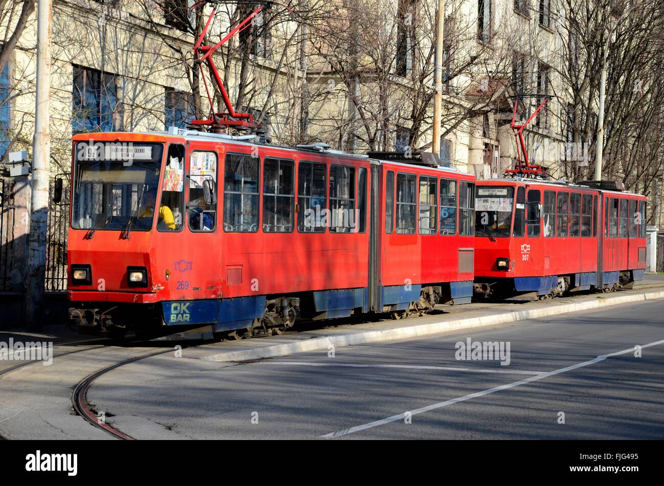 Belgrade weathered red tram trolley carriages in sunlight turns a bend ...