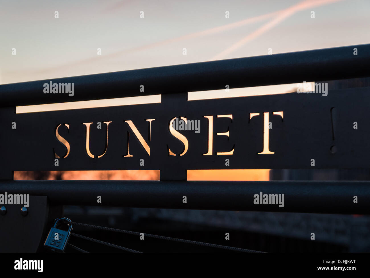 The word Sunset in a metal railing with a sunset glowing in the ...