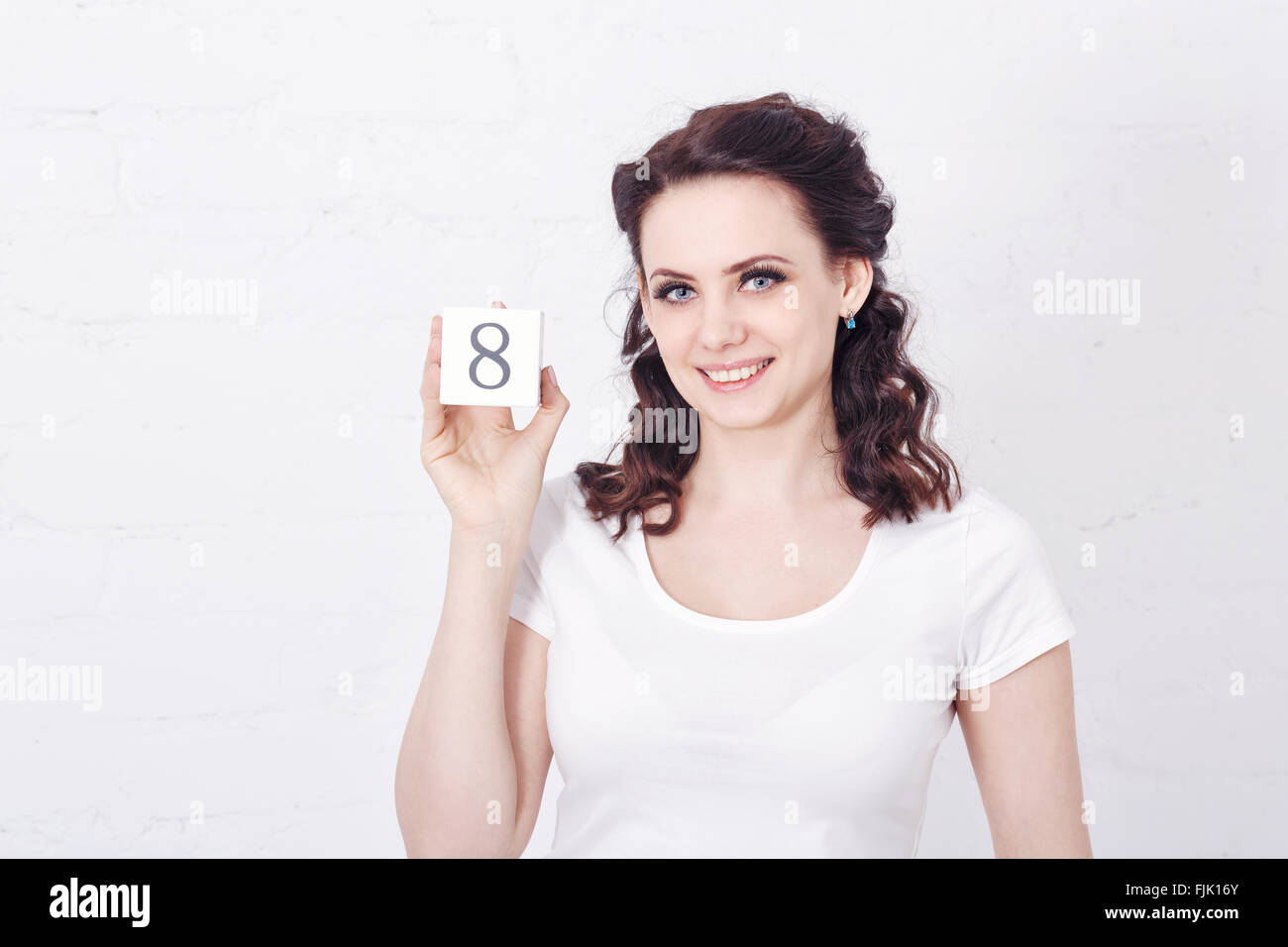 Young cute girl smiling and holding a number eight. Girl dressed in a ...