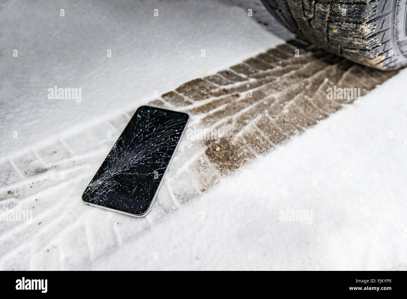 Phone with broken screen on snow in car trail. Glass covered with snow ...
