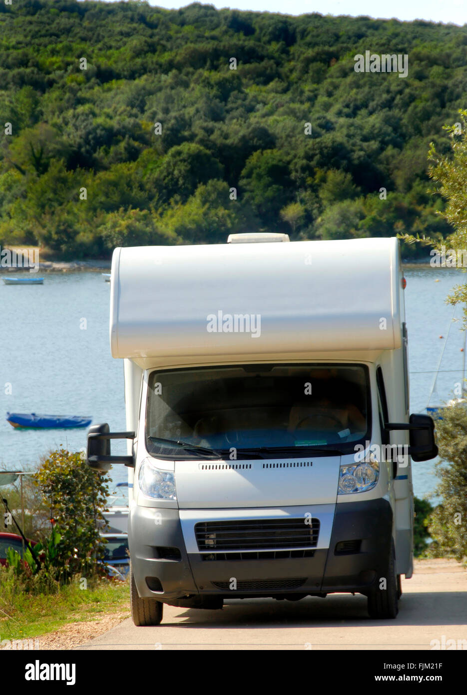 Camper on its way with at background a lake and trees Stock Photo - Alamy