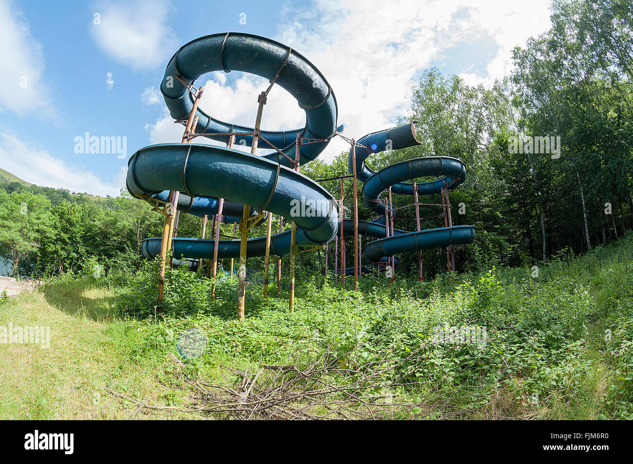 Abandoned water slide near a lake surrounded by trees. Small sunflare ...