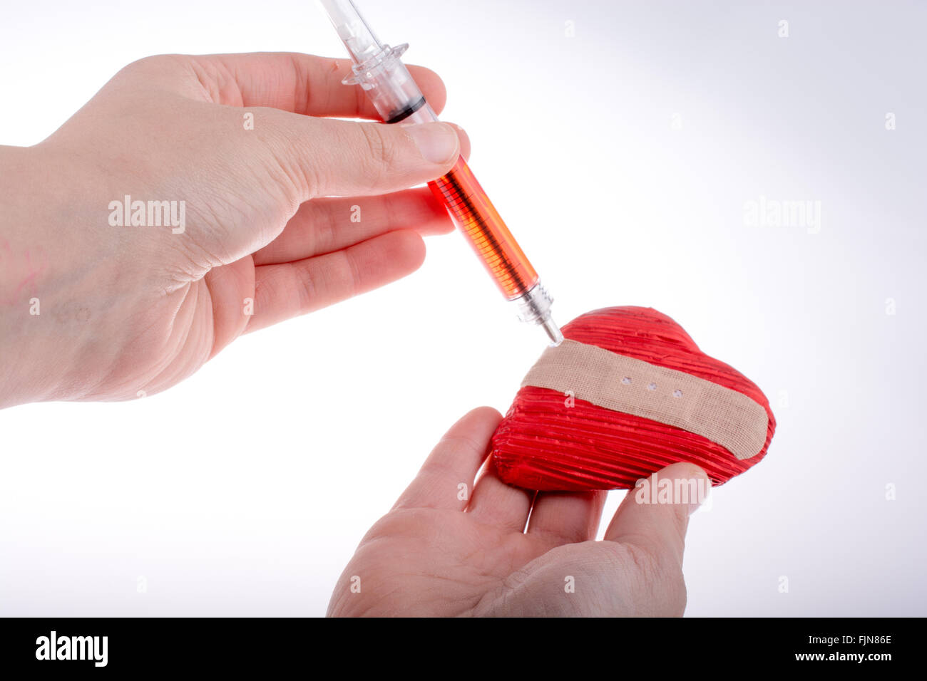 Hand injecting love into heart in plaster on white background Stock ...