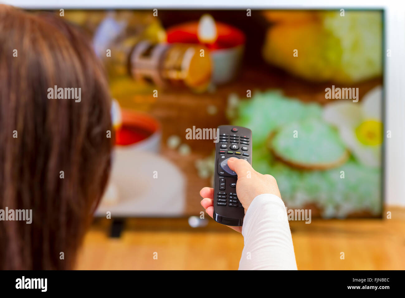 Over the shoulder view of girl sitting on sofa holding tv remote and ...