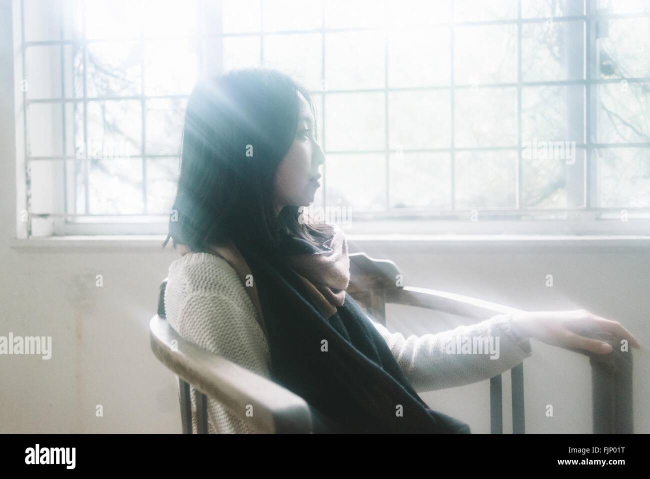 Young Woman Sitting On Chair Against Window At Home Stock Photo - Alamy
