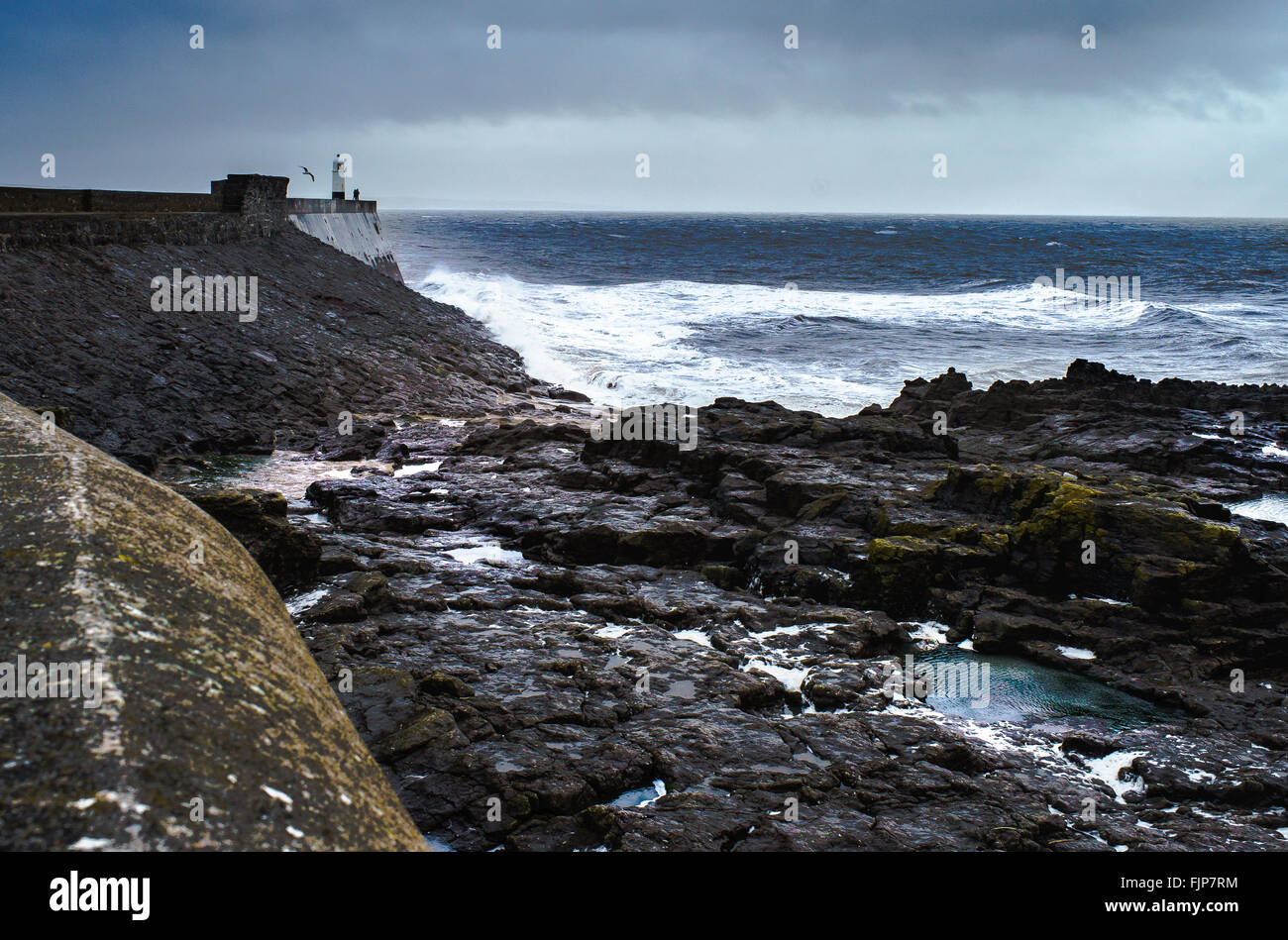 Wintry, dark seascape with waves crashing onto rocks and lighthouse ...