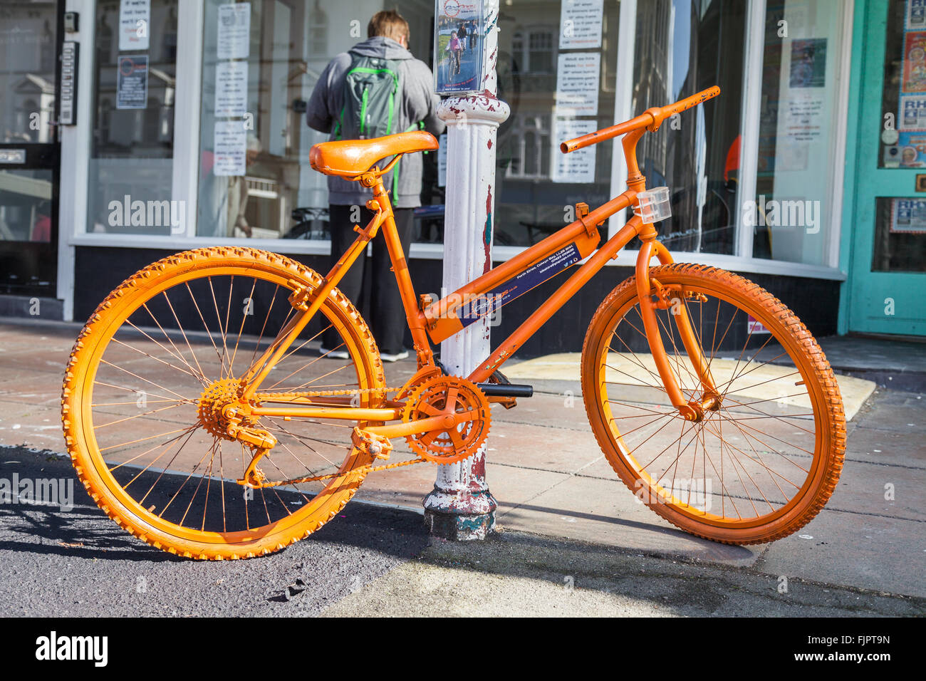 A bicycle painted completely orange chained to an iron post In Landudno ...