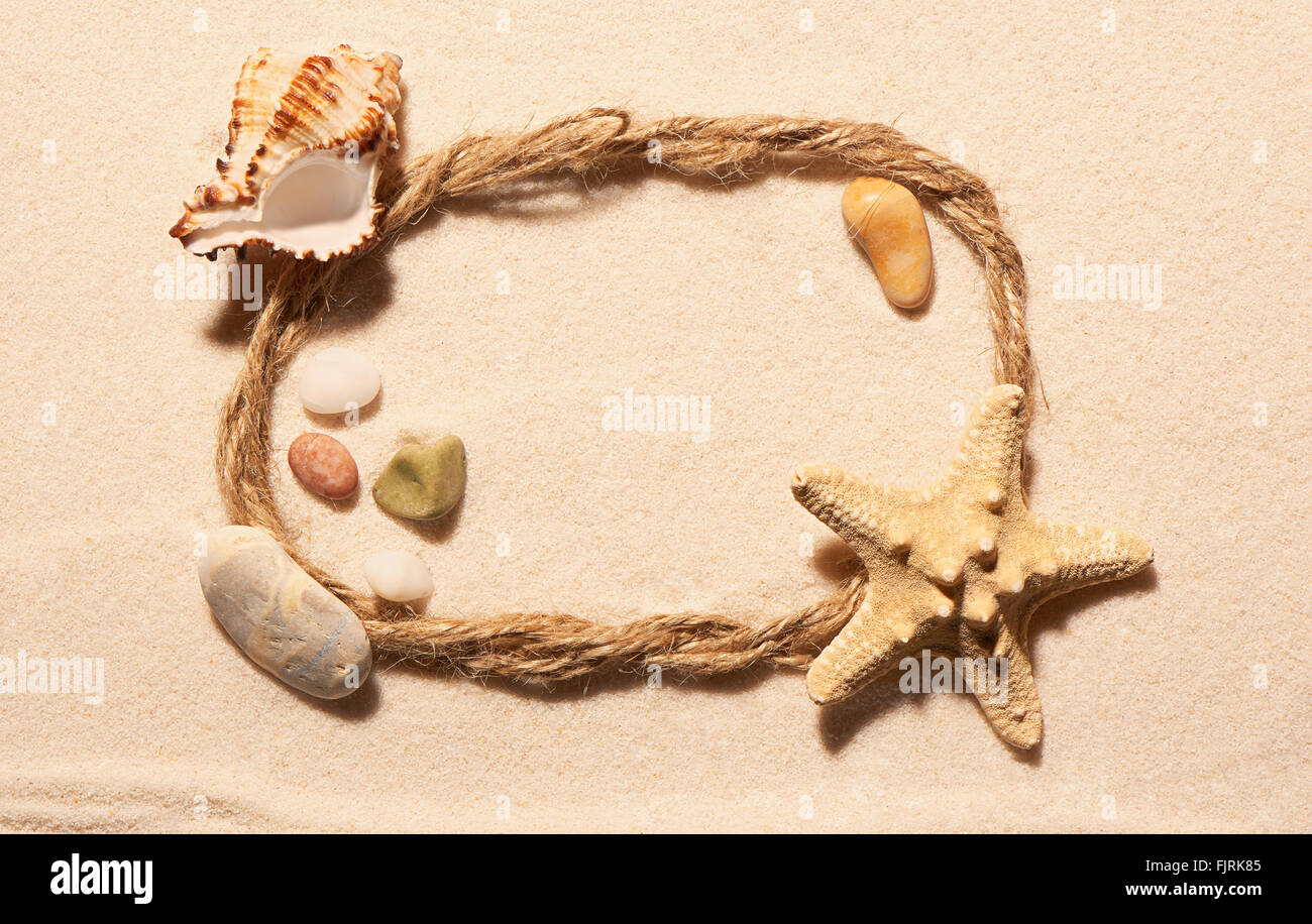 Oval frame of rope with starfish, empty sea shell and stones on sand ...
