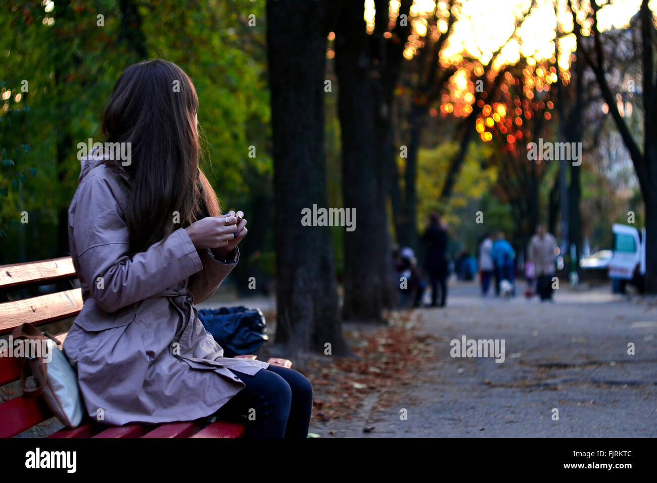 Girl sitting on the bench in park in the evening waiting for someone ...