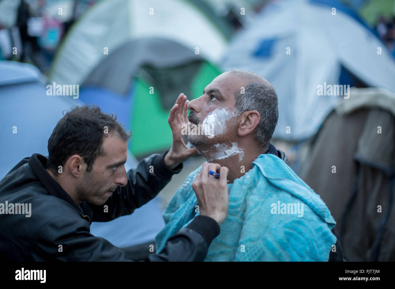 A Syrian barber shaves the beard of an Iranian customer next to tents ...
