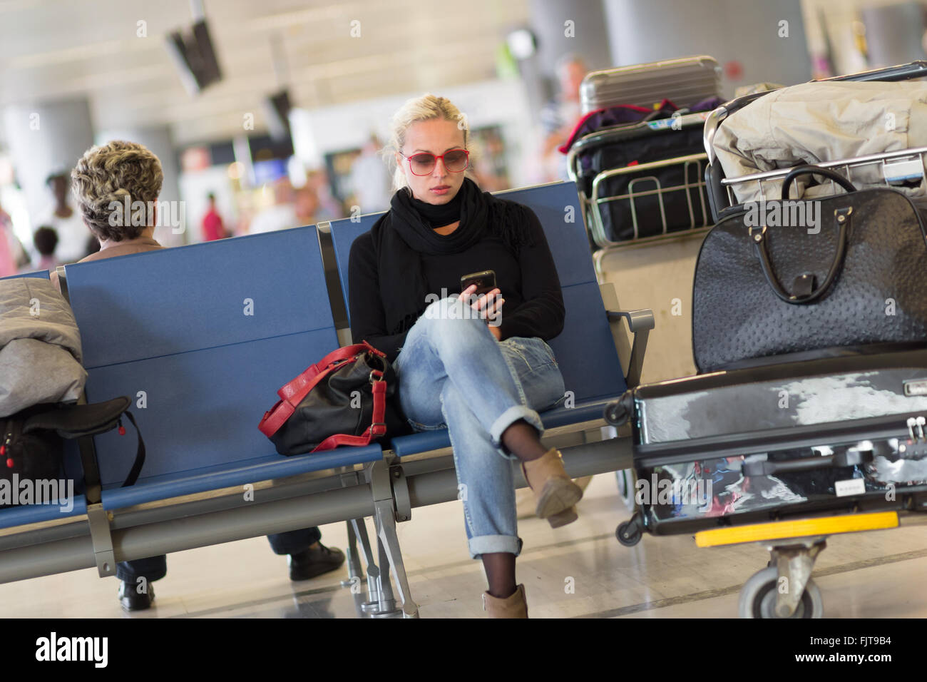 Female traveler using cell phone while waiting Stock Photo - Alamy