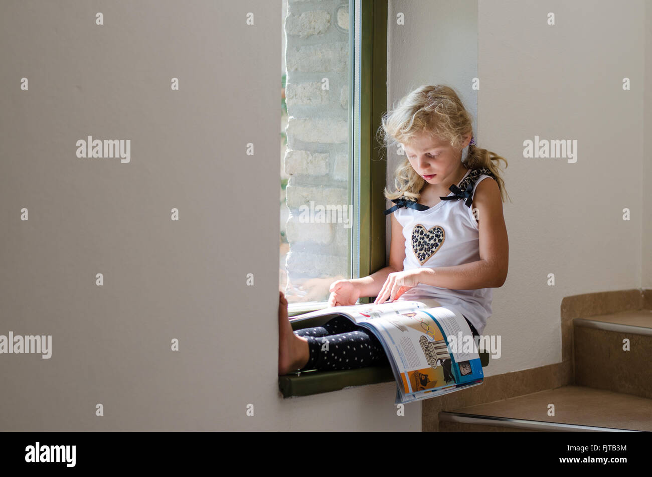 beautiful scholar blond girl sitting by the window and reading book ...