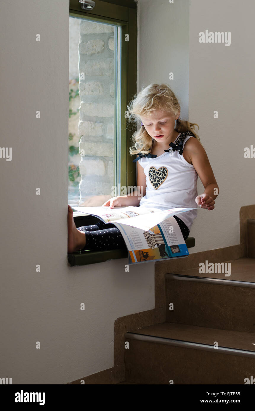 beautiful scholar blond girl sitting by the window and reading book ...
