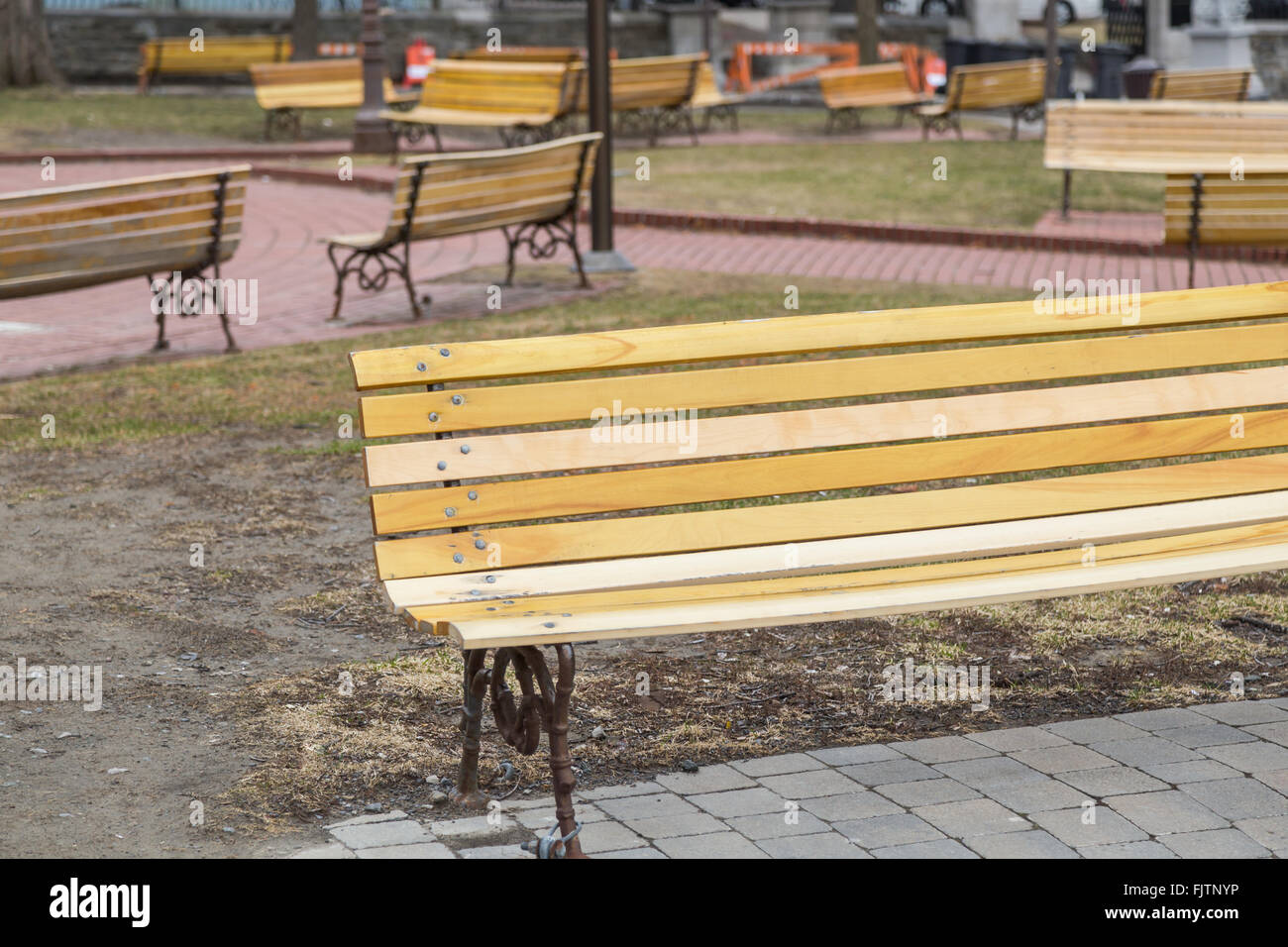 Scattered yellow wooden benches on interlocking pavement in a park in ...