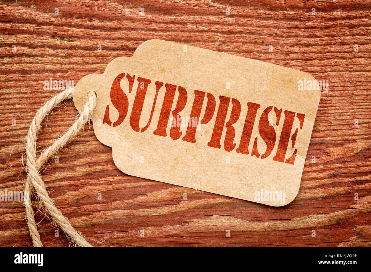 surprise red stencil text on a paper price tag against rustic wood ...