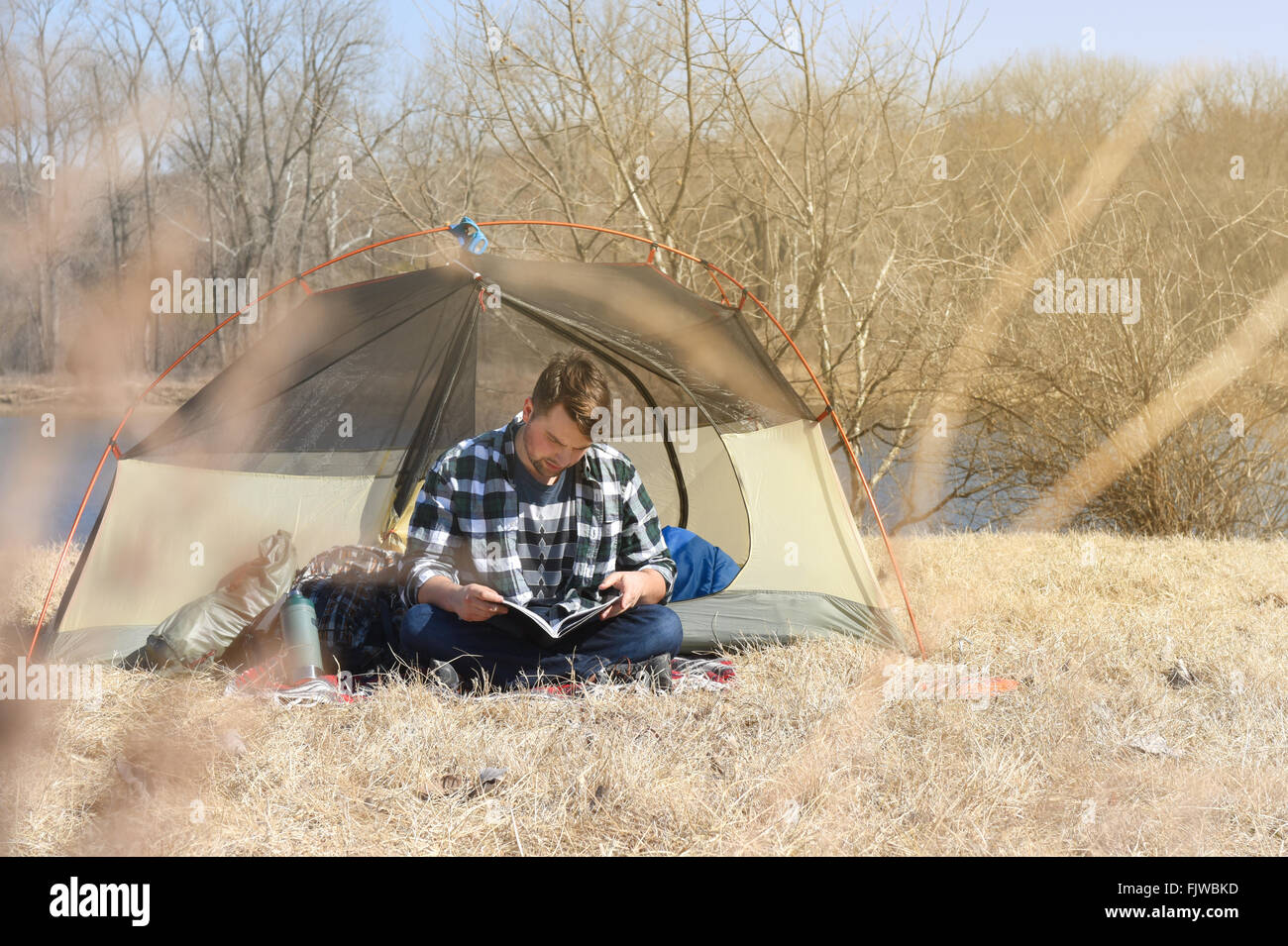 Young man reading seating outside camping tent Stock Photo - Alamy