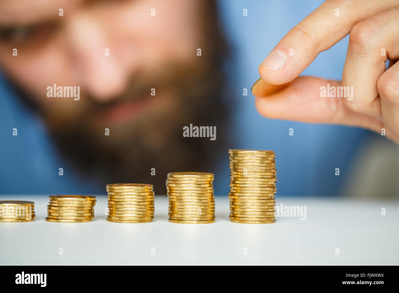 Savings, beared man stacking gold coins into increasing columns Stock ...