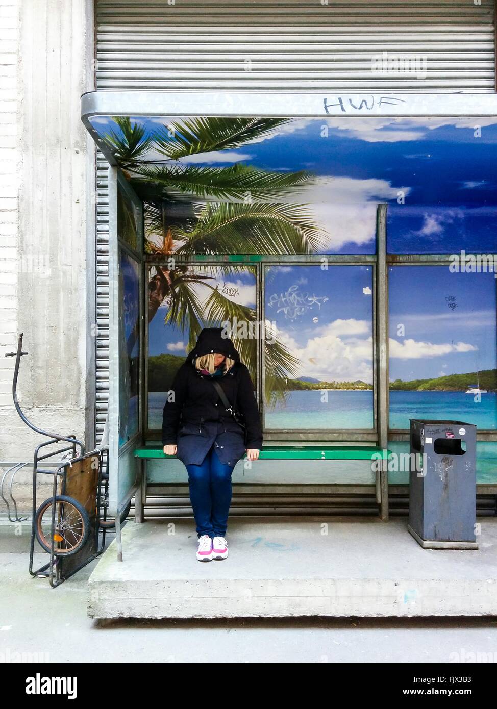 Front View Of Hooded Woman Sitting On Bench By Building Stock Photo - Alamy