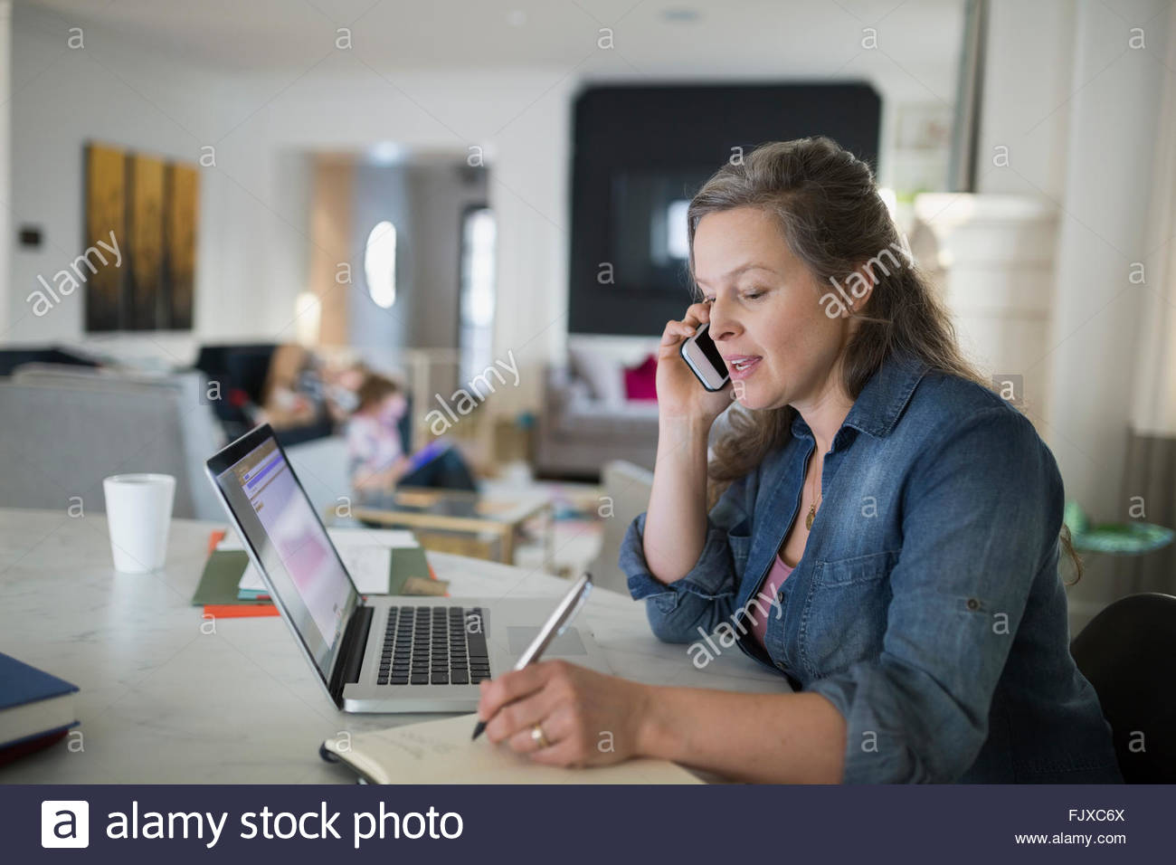 Woman talking on cell phone laptop at table Stock Photo - Alamy
