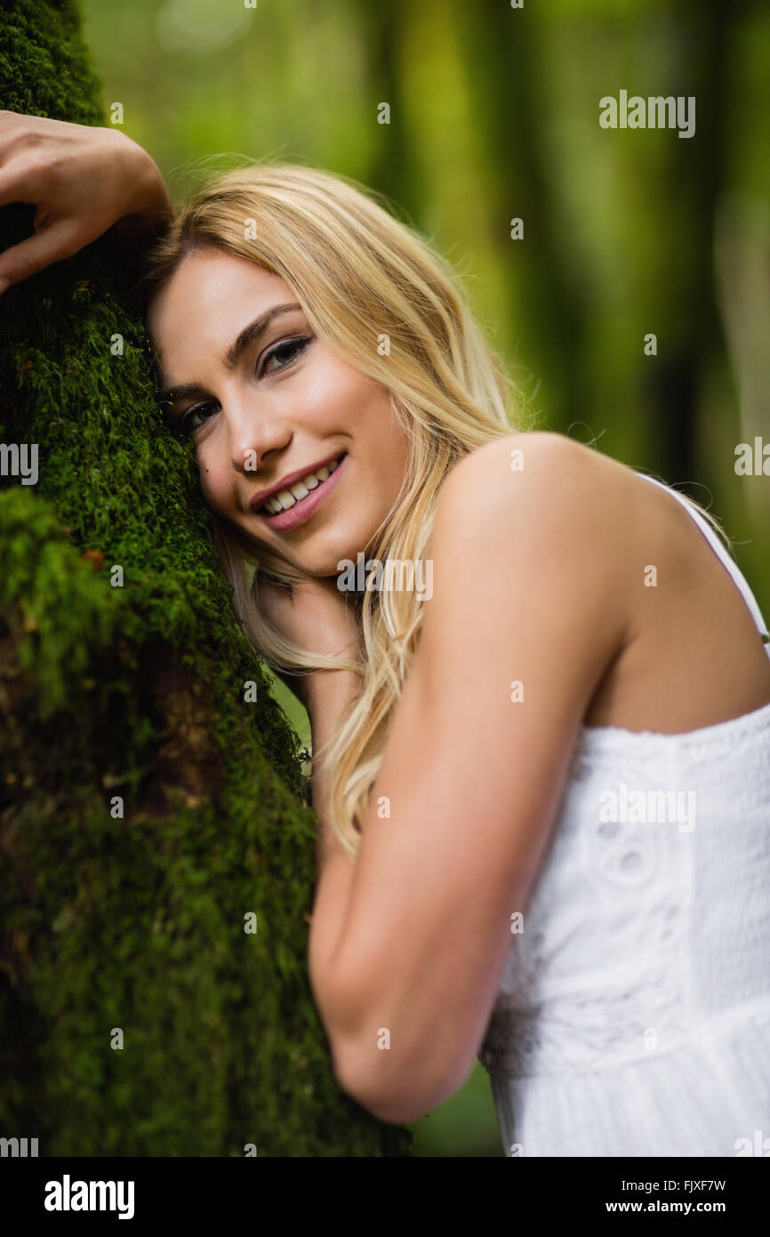 Beautiful blonde woman standing next to a tree trunk Stock Photo - Alamy