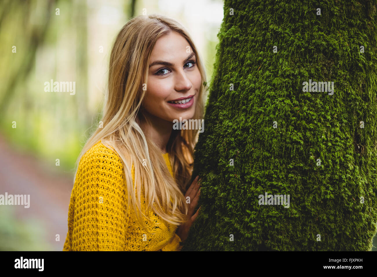 Beautiful blonde woman standing next to a tree trunk Stock Photo - Alamy