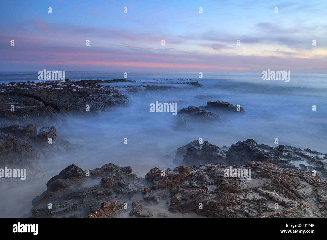 Long exposure of sunset over rocks, giving a mist like effect over ...