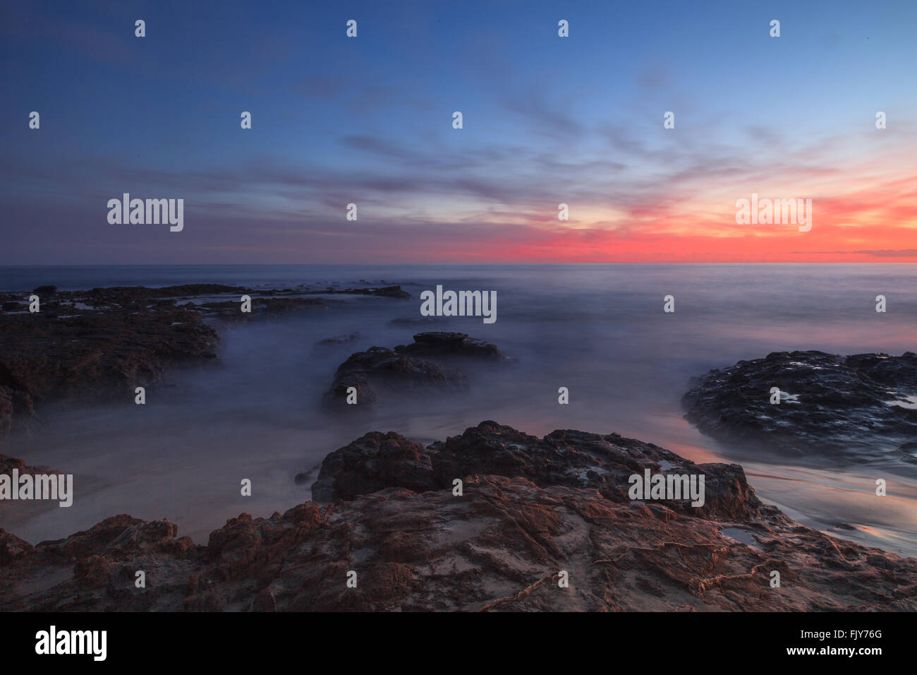 Long exposure of sunset over rocks, giving a mist like effect over ...