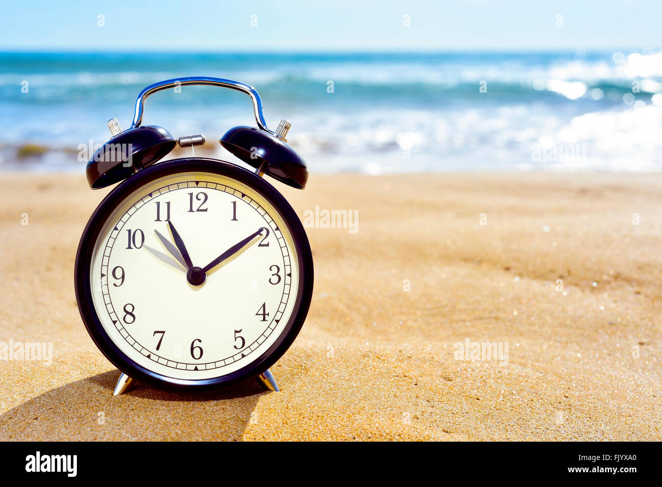 closeup of an alarm clock on the sand of a beach adjusting forward one ...