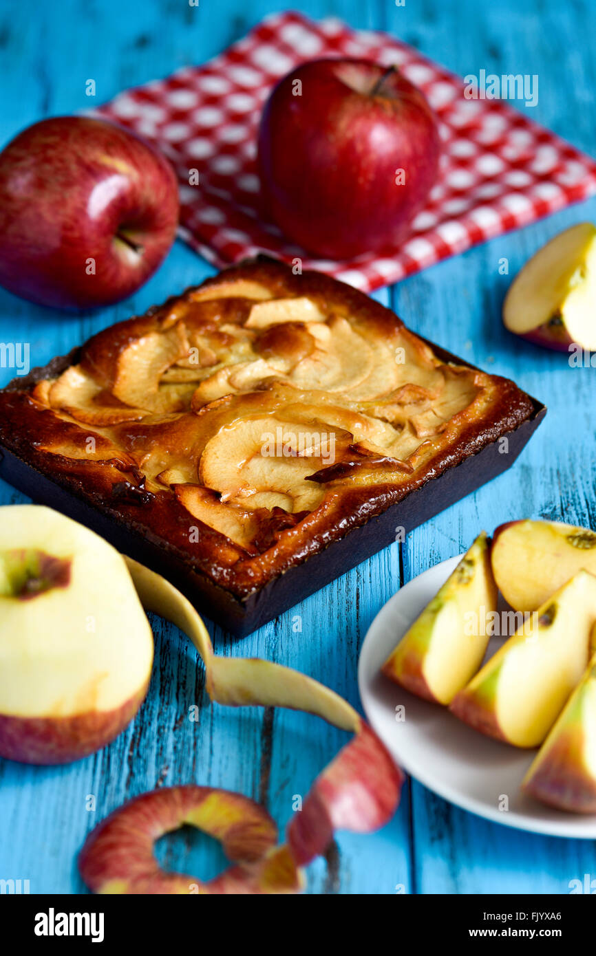 closeup of an apple cake and some red apples on a blue rustic wooden ...