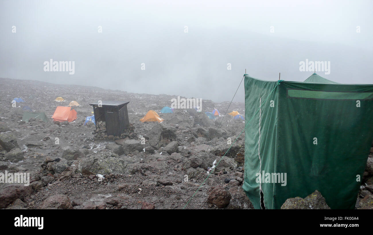 A canvas portable toilet and tents set up amongst large lava rocks at ...