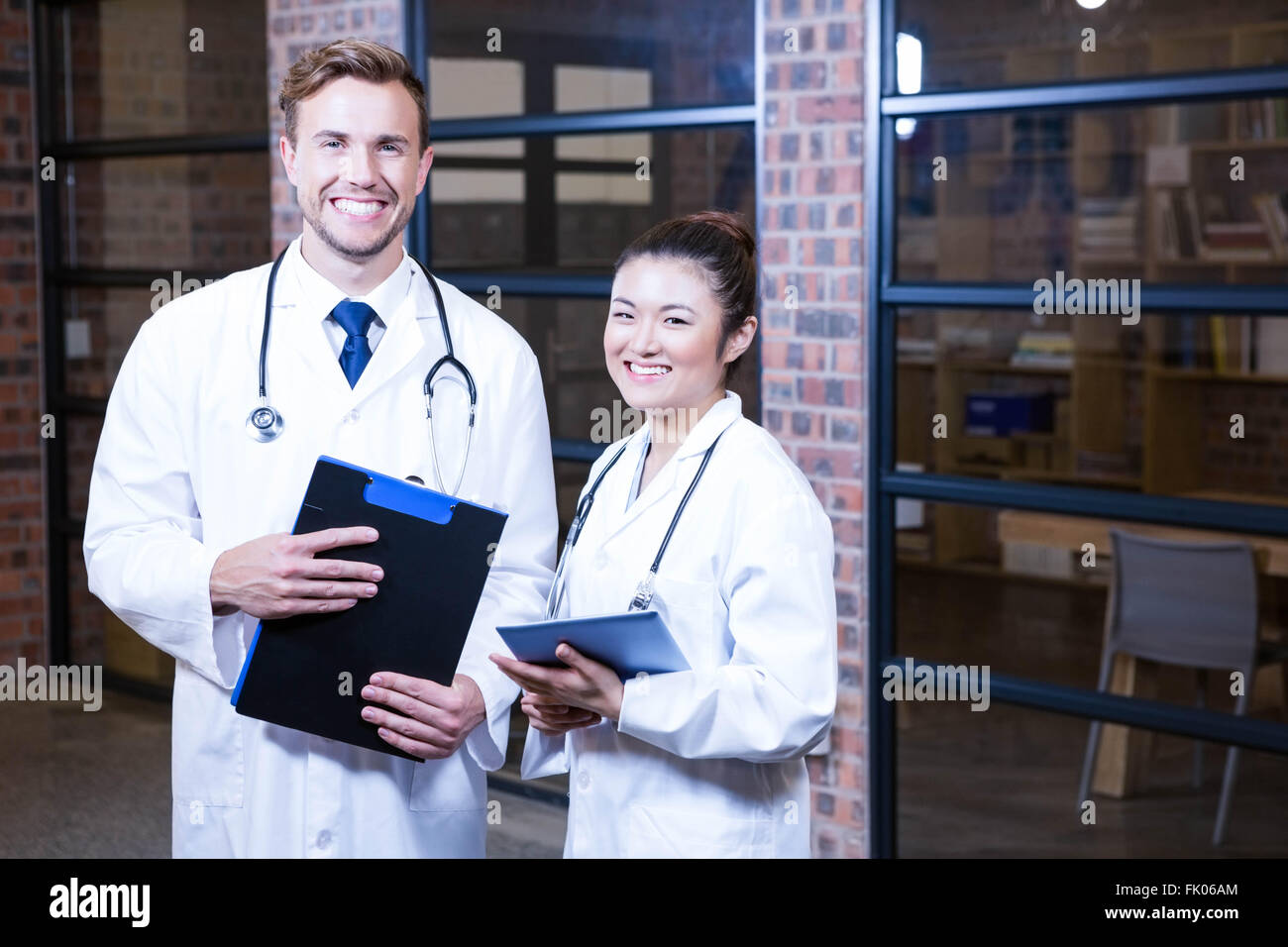 Portrait of doctors standing near library with clipboard and digital ...