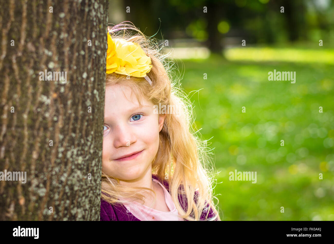 beautiful blond girl behing tree in a park Stock Photo - Alamy