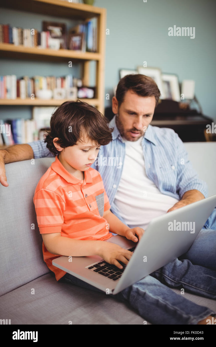 Serious father and son using laptop while sitting on sofa Stock Photo ...