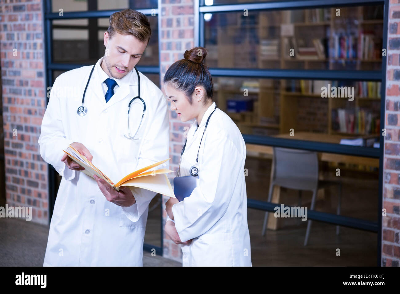 Two doctors looking at file and discussing near library Stock Photo - Alamy