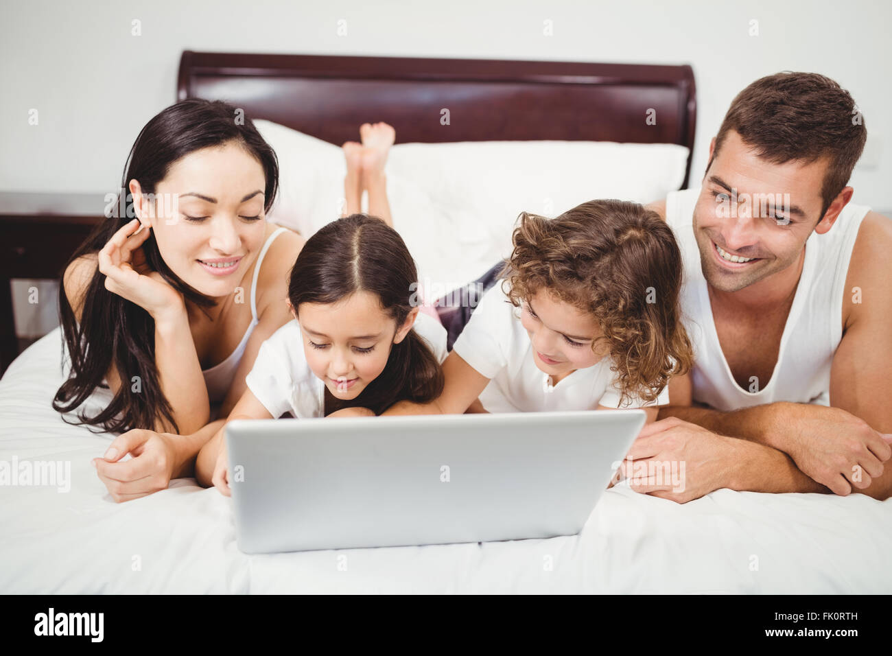 Happy children with parents using laptop on bed Stock Photo - Alamy