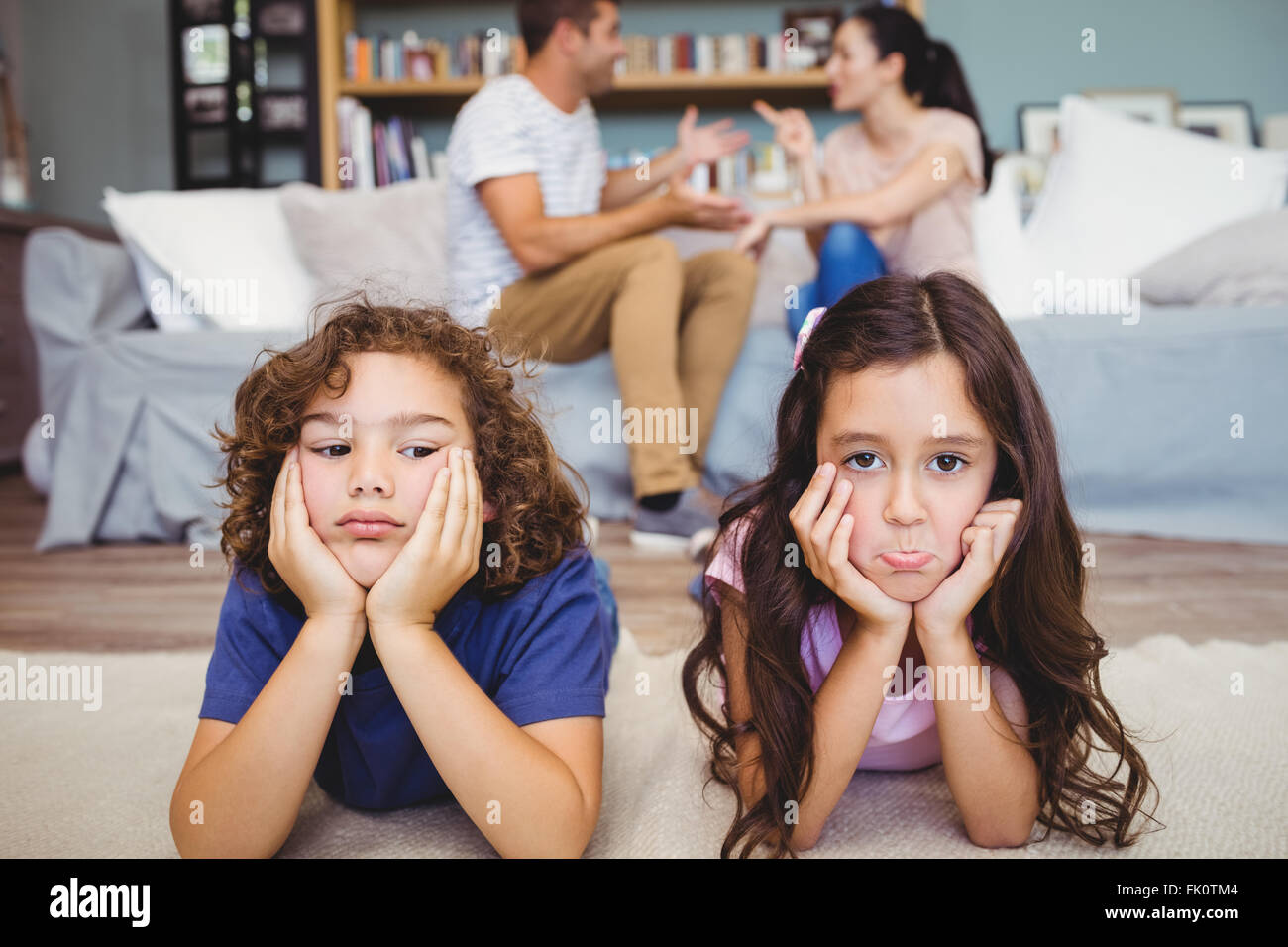 Sad siblings lying on carpet while parents sitting in background Stock ...