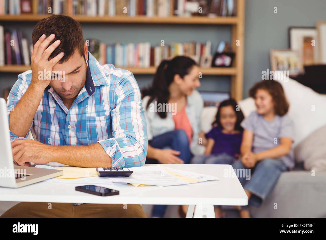 Tensed man by laptop while family sitting in background Stock Photo - Alamy