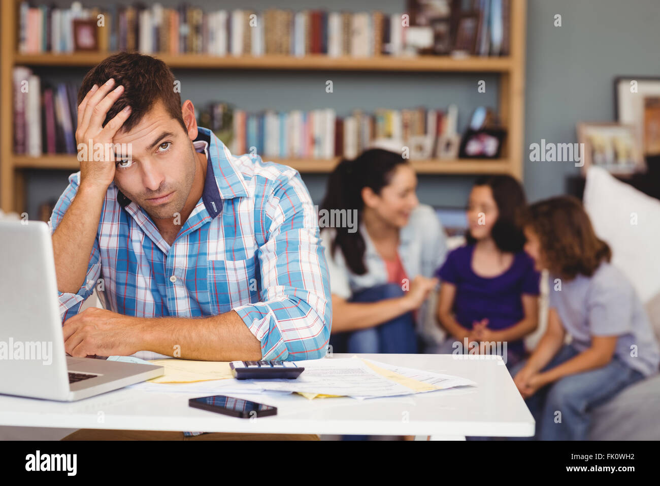 Tensed man by laptop table while family sitting in background Stock ...