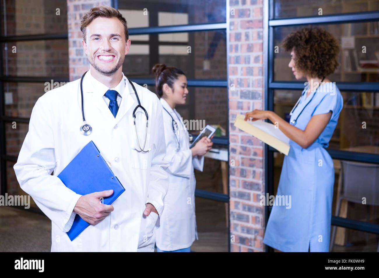 Male doctor standing near library with clipboard Stock Photo - Alamy