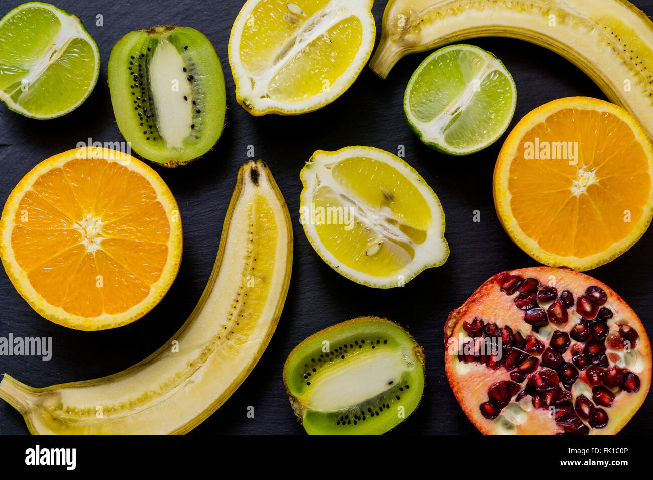 Top view showing many fruits sliced in half on a dark background ...