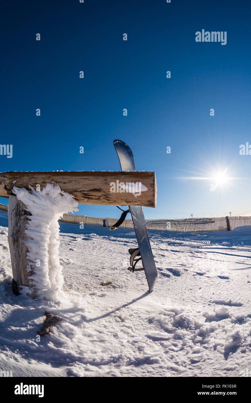 Snowboard leaning on a wood rail on a winter snow covered mountainside ...