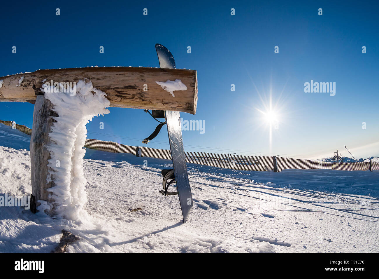 Snowboard leaning on a wood rail on a winter snow covered mountainside ...